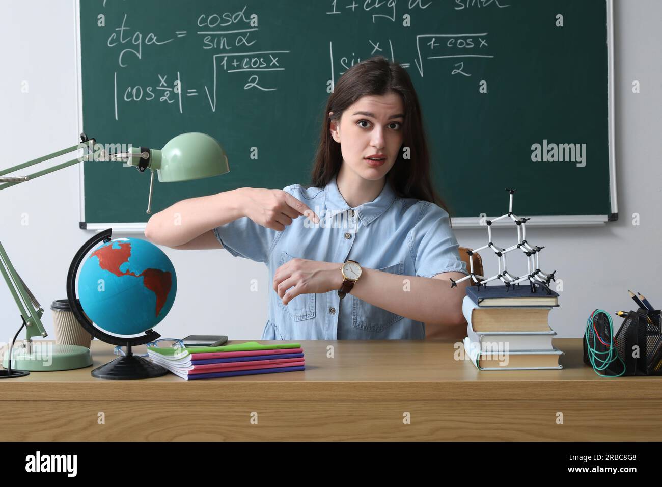 Female teacher pointing at wristwatch in classroom Stock Photo - Alamy