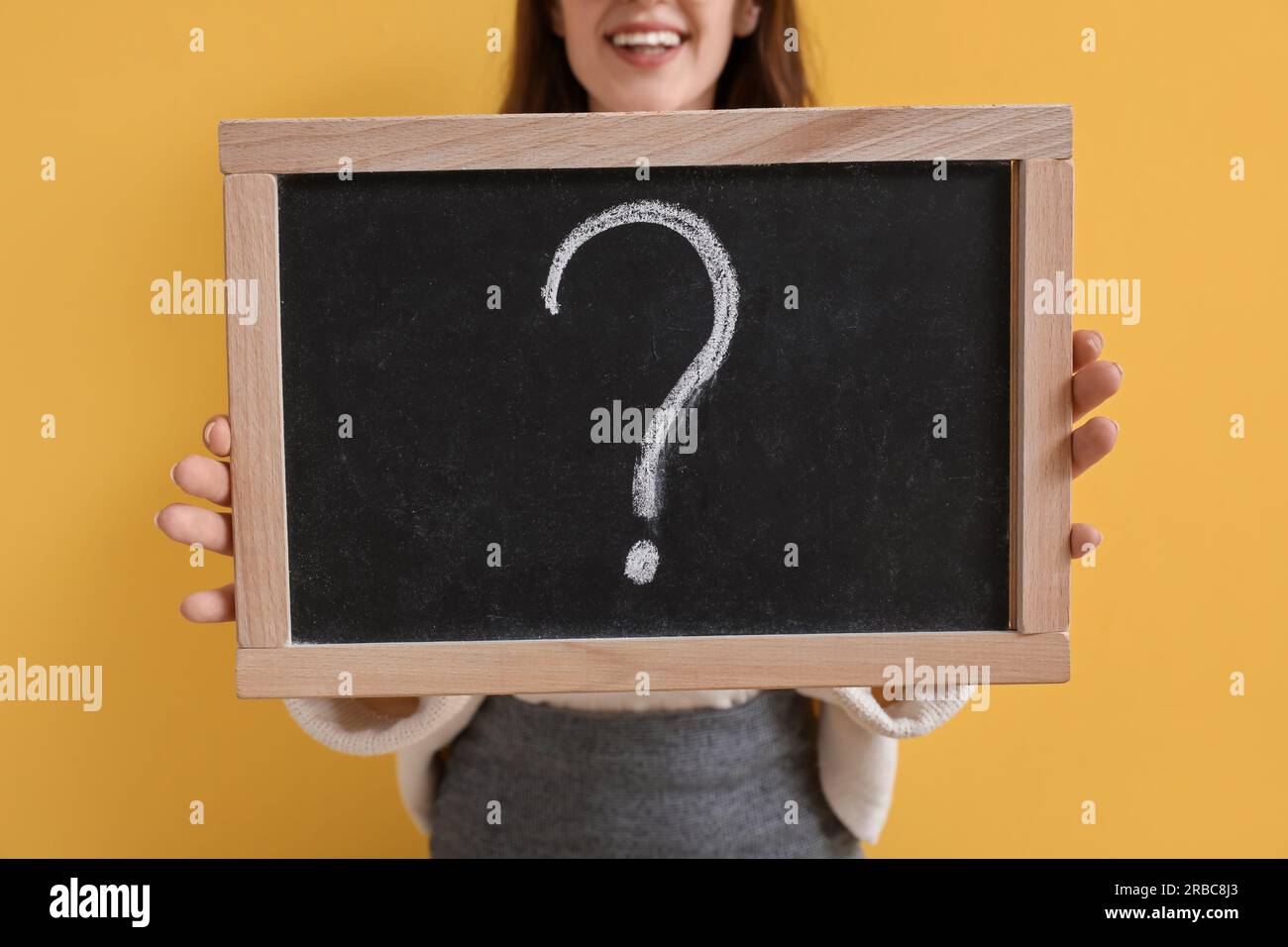 Female teacher holding chalkboard with question mark on yellow ...