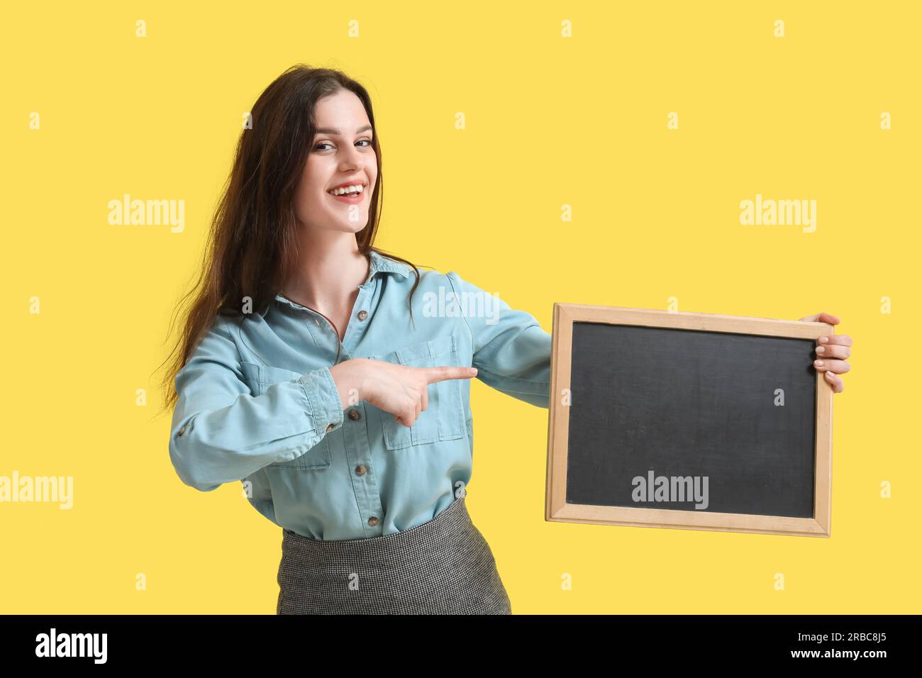 Female teacher pointing at chalkboard on yellow background Stock Photo ...