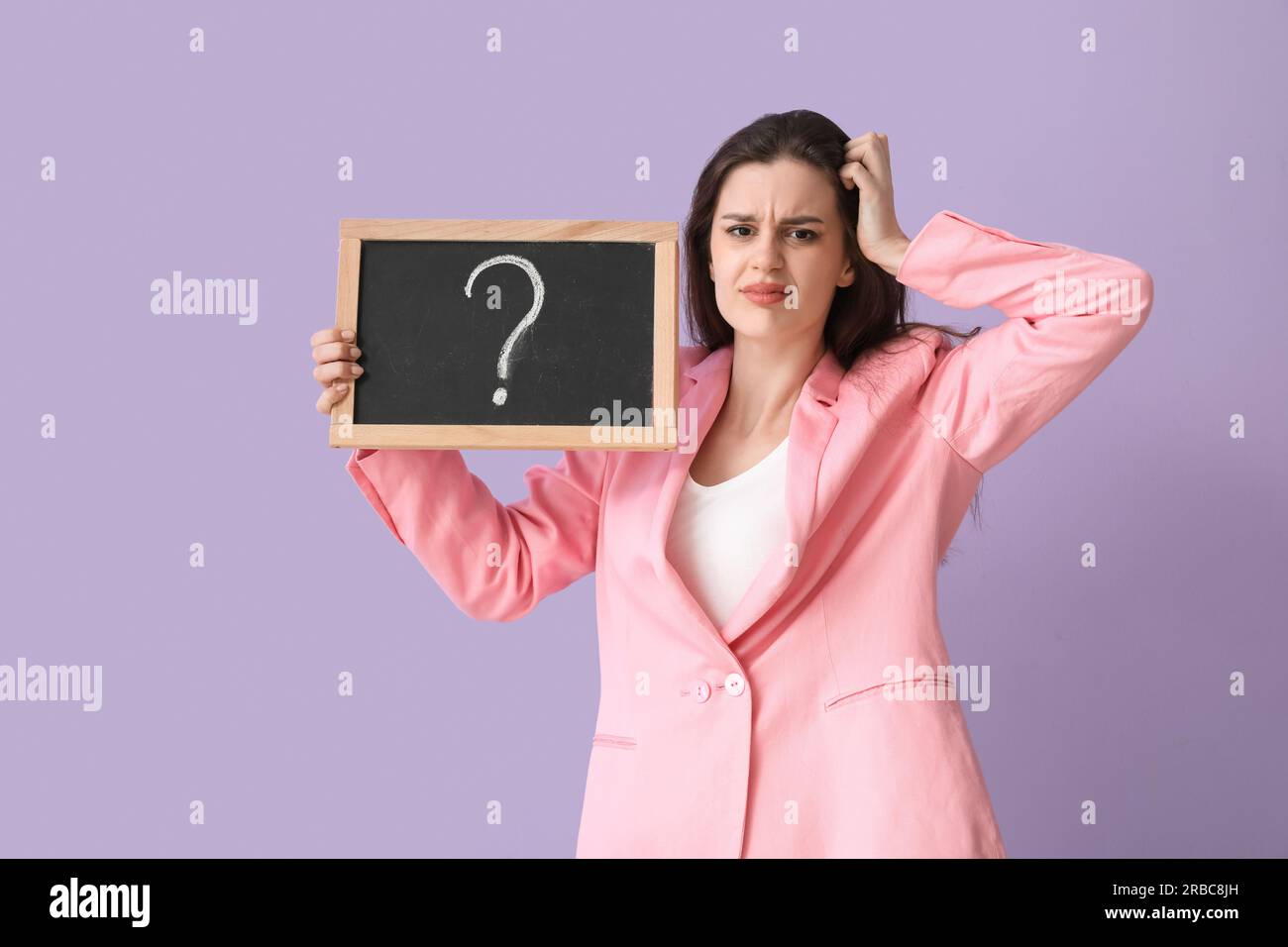 Stressed female teacher holding chalkboard with question mark on lilac ...