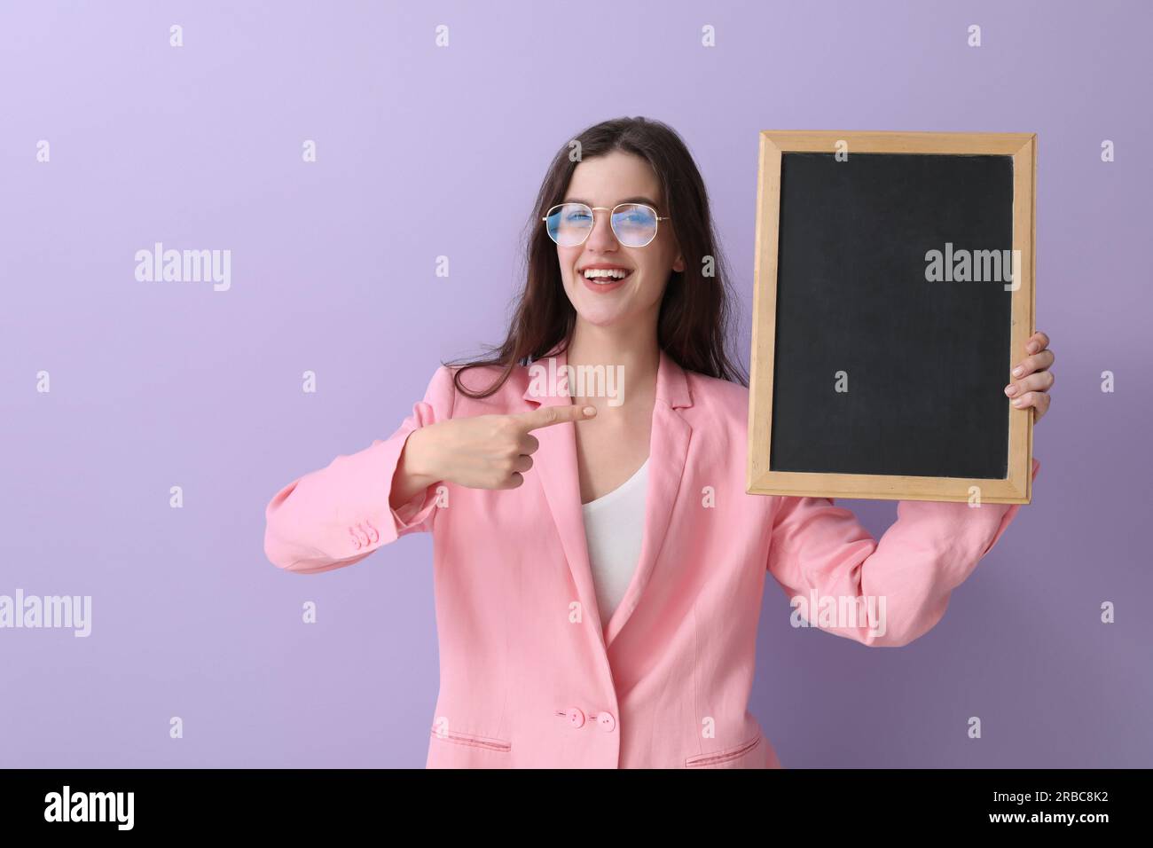 Female teacher pointing at chalkboard on lilac background Stock Photo ...
