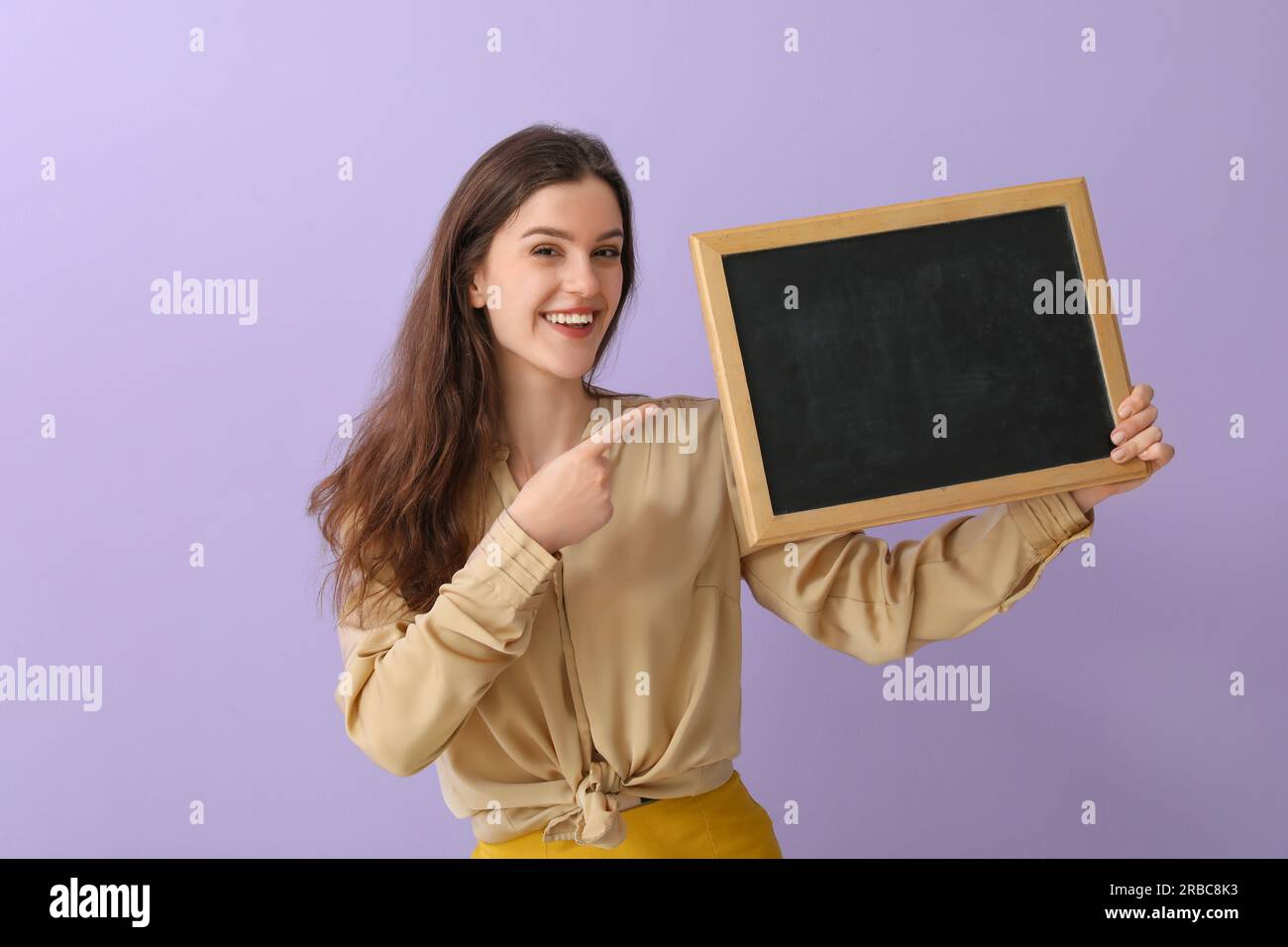 Female teacher pointing at chalkboard on lilac background Stock Photo ...