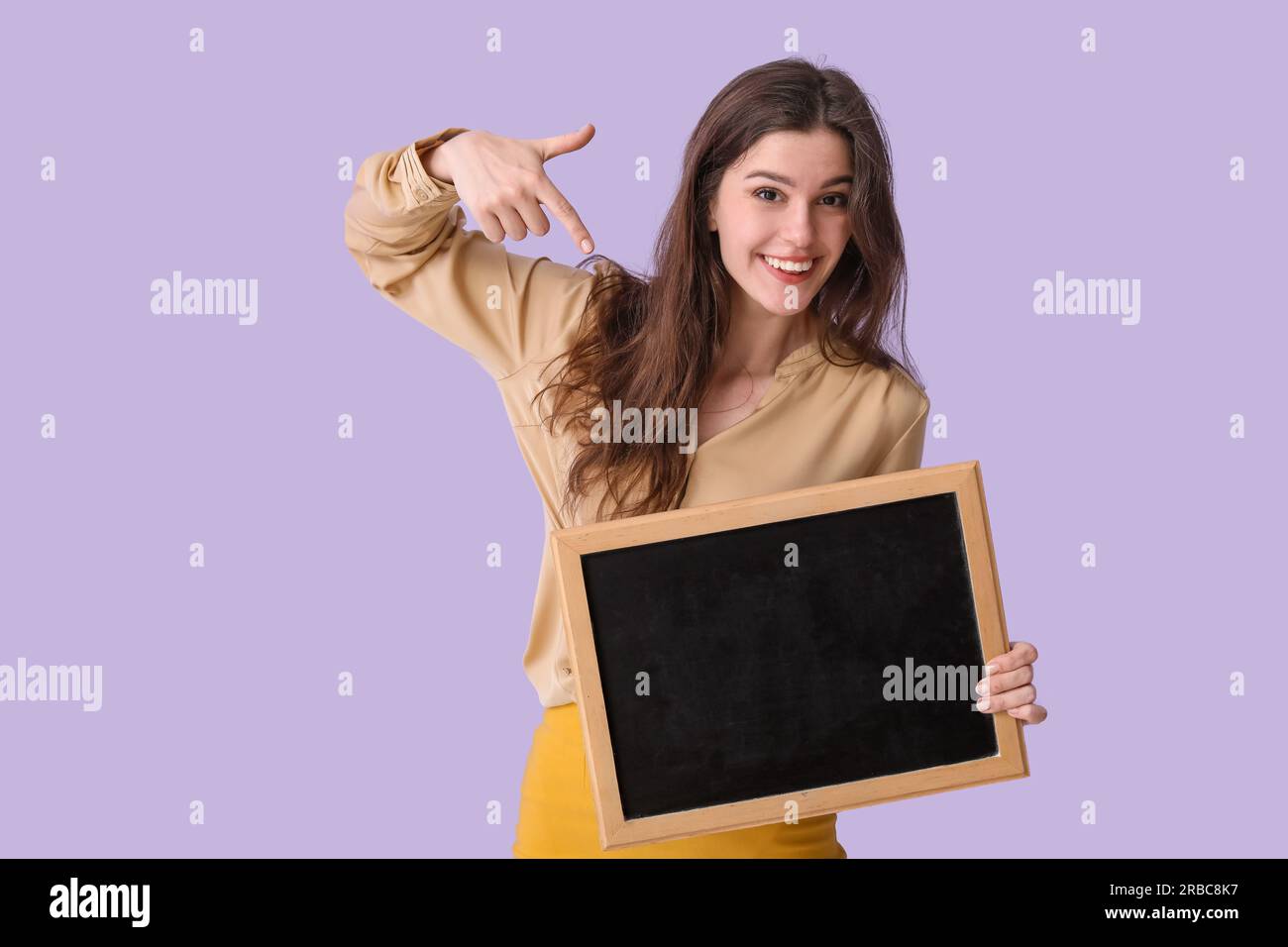 Female teacher pointing at chalkboard on lilac background Stock Photo ...