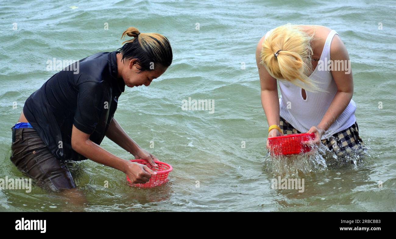 Two young women use plastic sieves to sieve the sea, hoping to collect ...