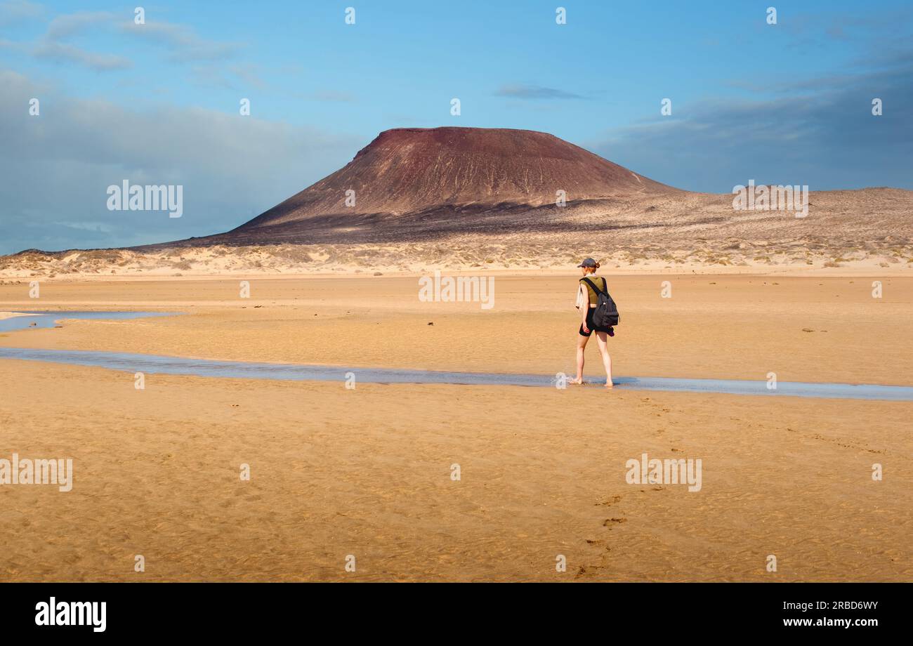 Young woman walking through desert and sand dunes with volcano in ...