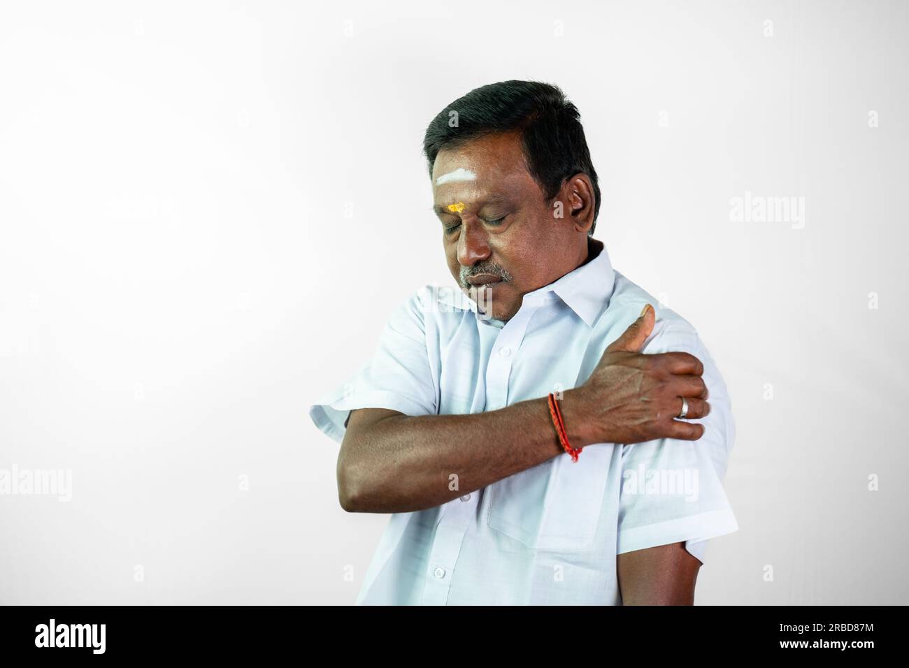 holding his right shoulder. He is wearing a white dress shirt and a ...