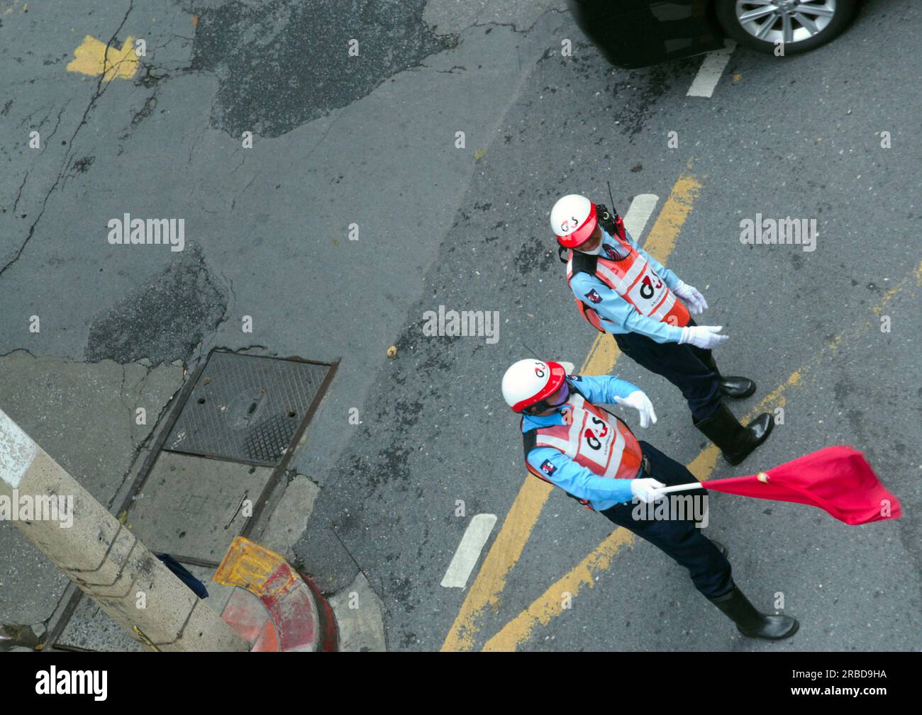 Overhead view of two male security guards, one holding a red flag ...
