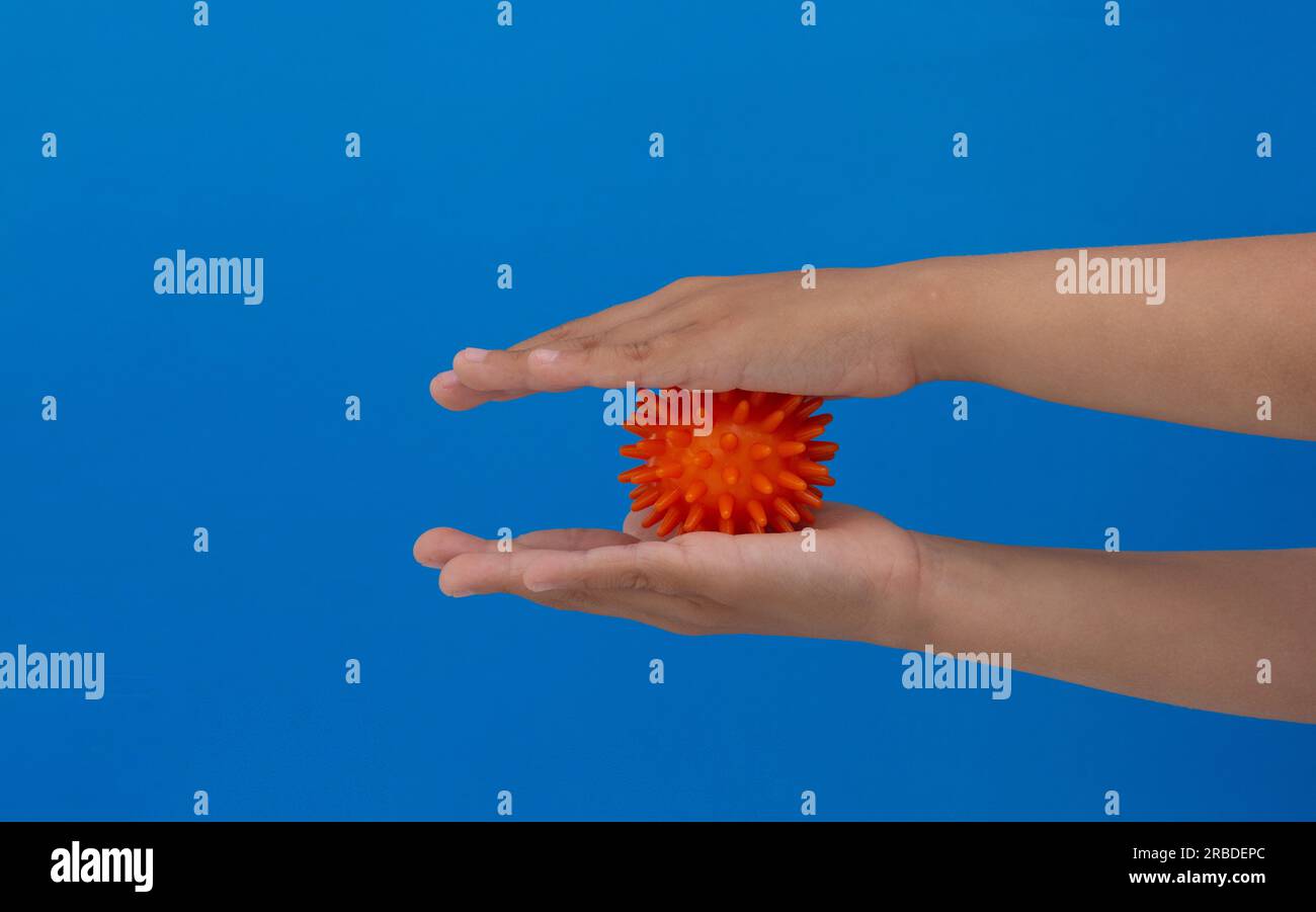 Child hands rolling spiky orange massage needle ball between palms over ...