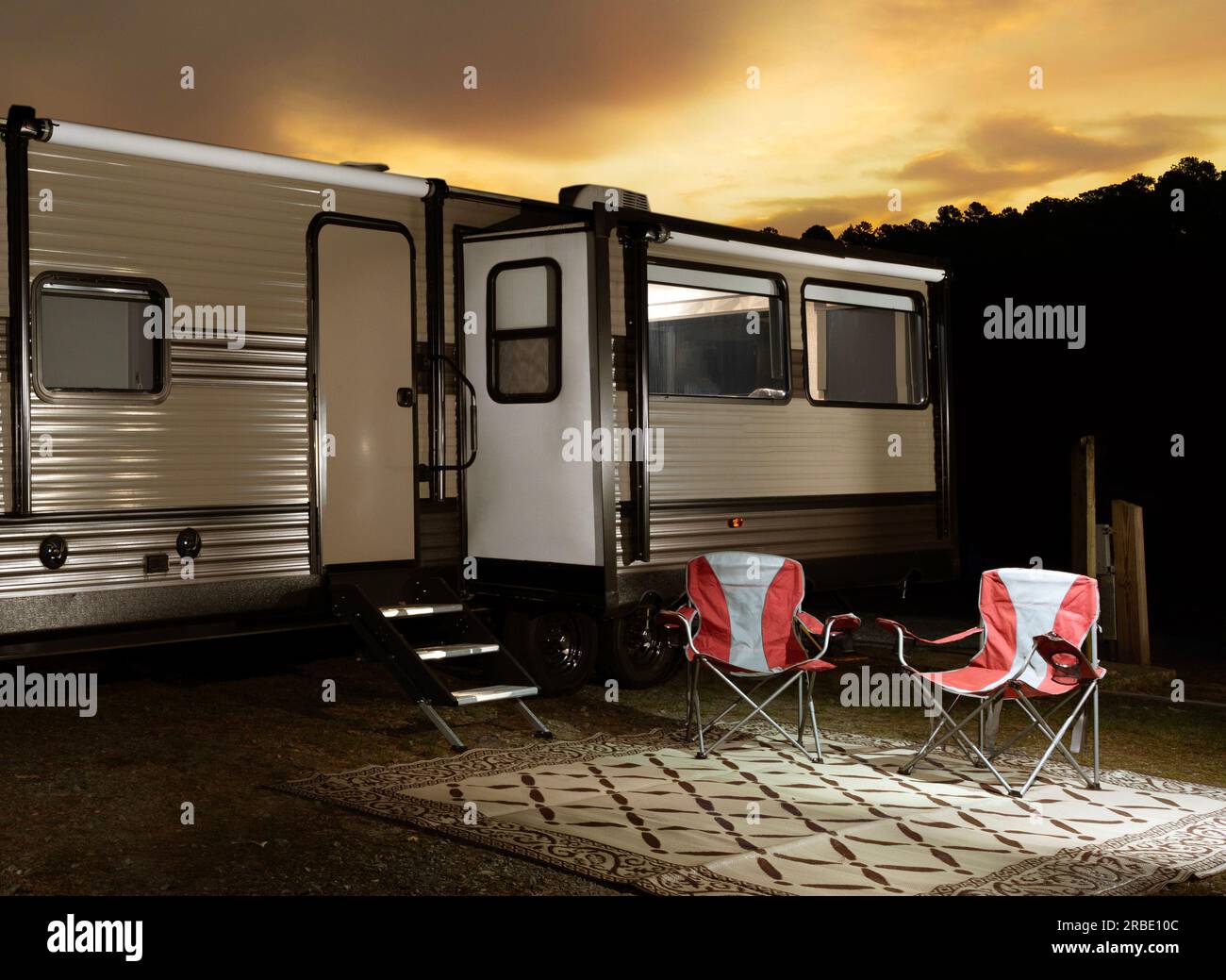 Two red chairs behind a travel trailer with colorful sunset going down ...