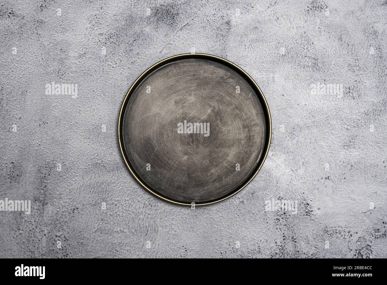 A vintage metal circular plate with a gold edge on a grainy surface ...