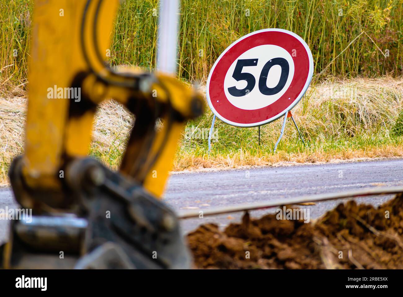 Arm of a mini digger and bucket with a speed limit sign at 50, road ...