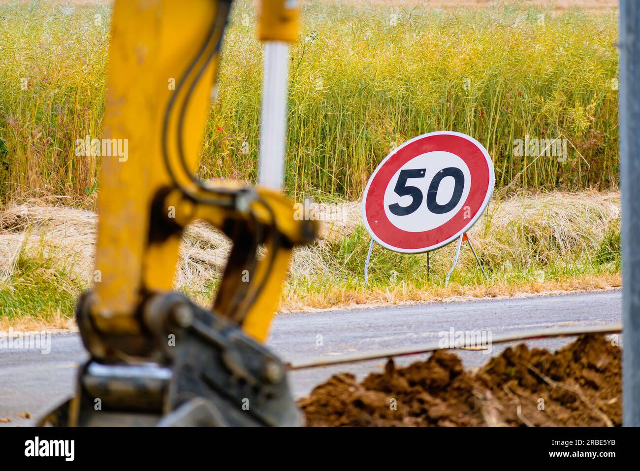 Arm of a mini digger and bucket with a speed limit sign at 50, road ...