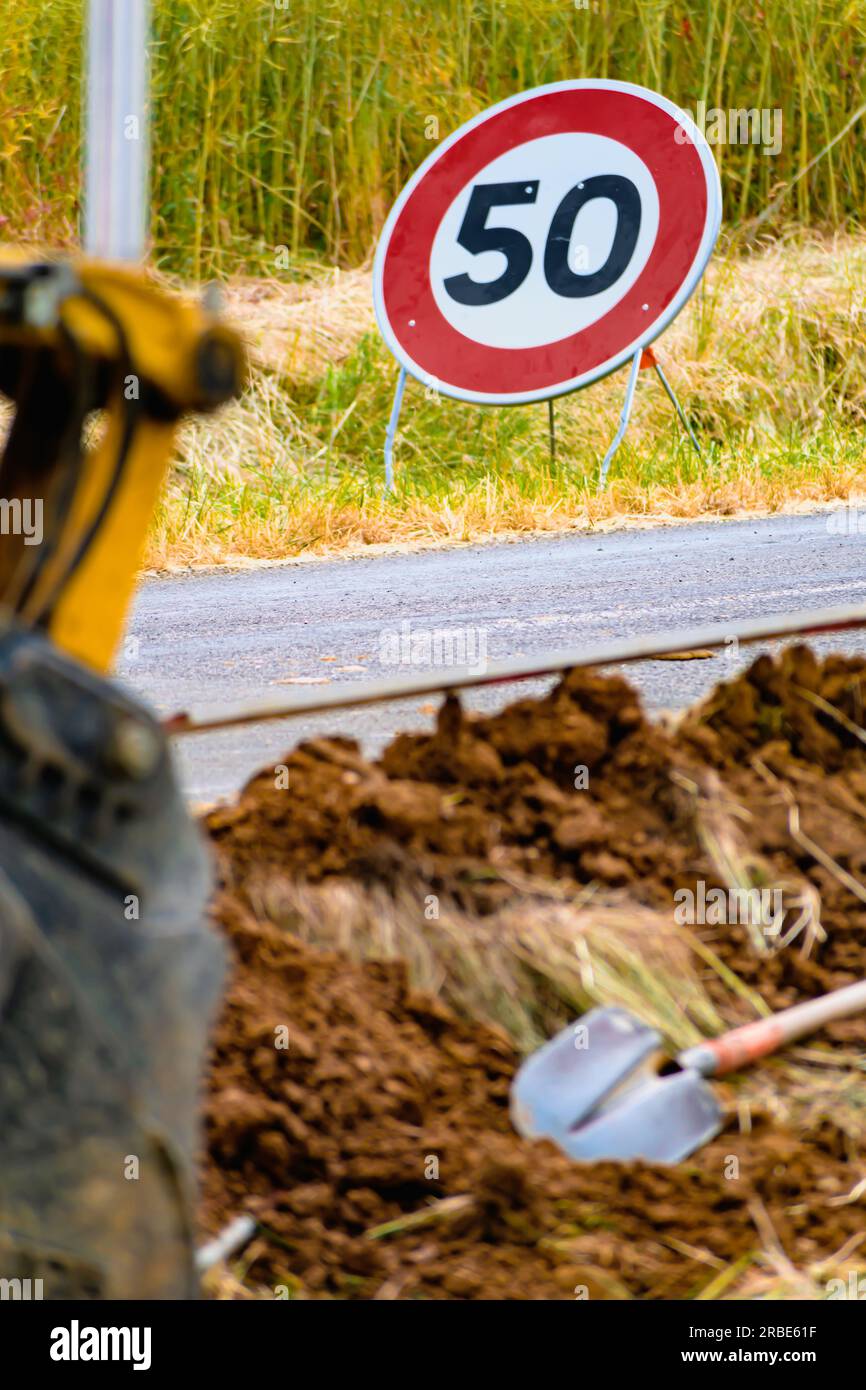 Arm of a mini digger and bucket with a speed limit sign at 50, road ...