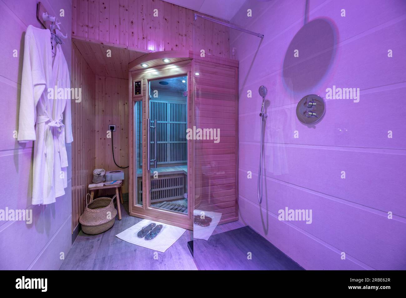 A room with a small wooden Finnish sauna with a glass door, an outdoor ...