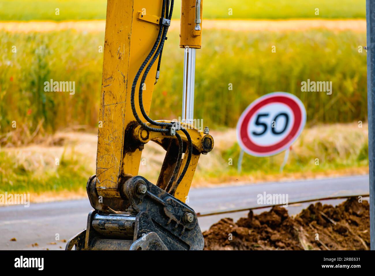 Arm of a mini digger and bucket with a speed limit sign at 50, road ...