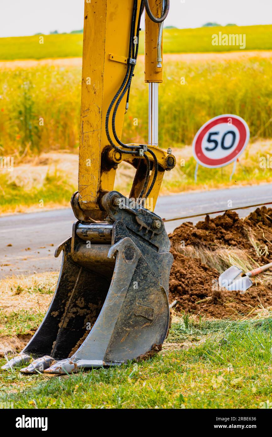 Arm of a mini digger and bucket with a speed limit sign at 50, road ...
