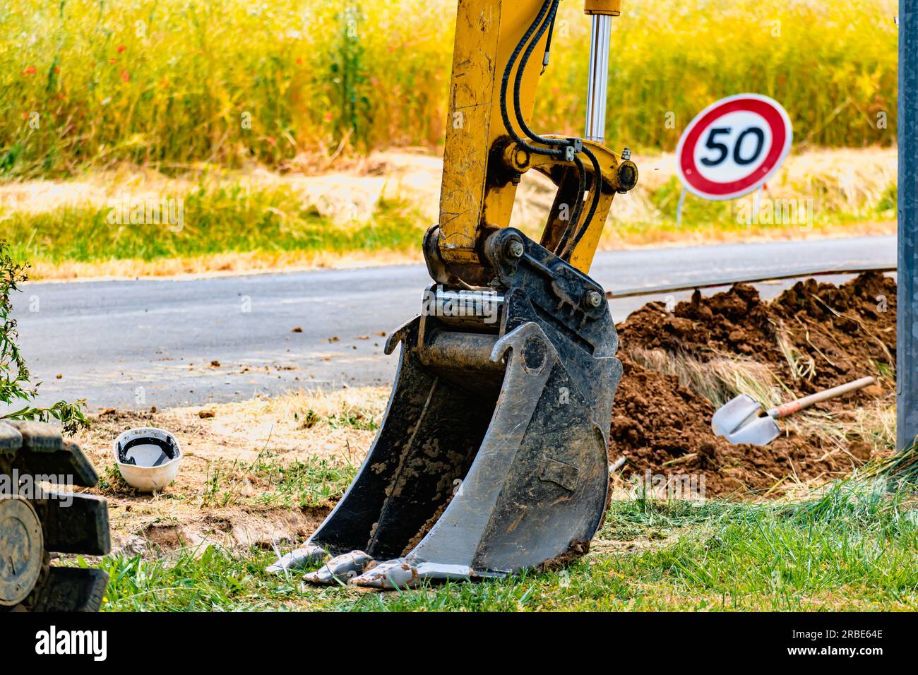 Arm of a mini digger and bucket with a speed limit sign at 50, road ...