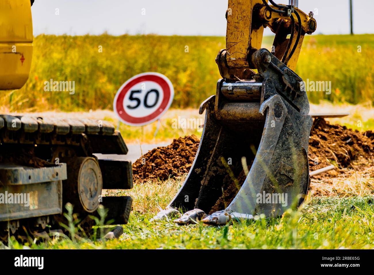 Arm of a mini digger and bucket with a speed limit sign at 50, road ...