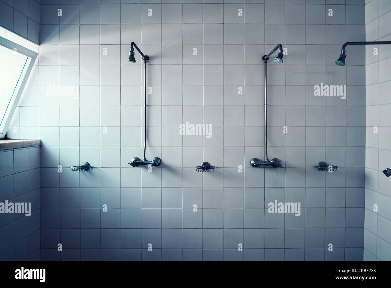 Public empty shower room with white tiles in a gym with light coming ...