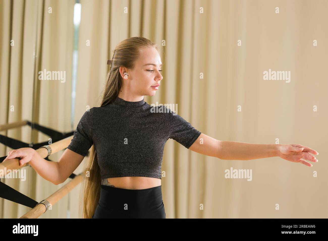Young woman ballerina stretching and training at barre in dance studio ...