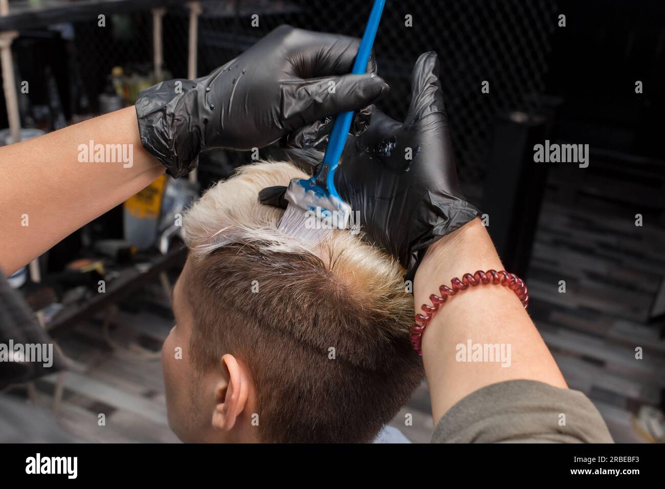 The hands of a professional barber girl in gloves dye hair roots white ...