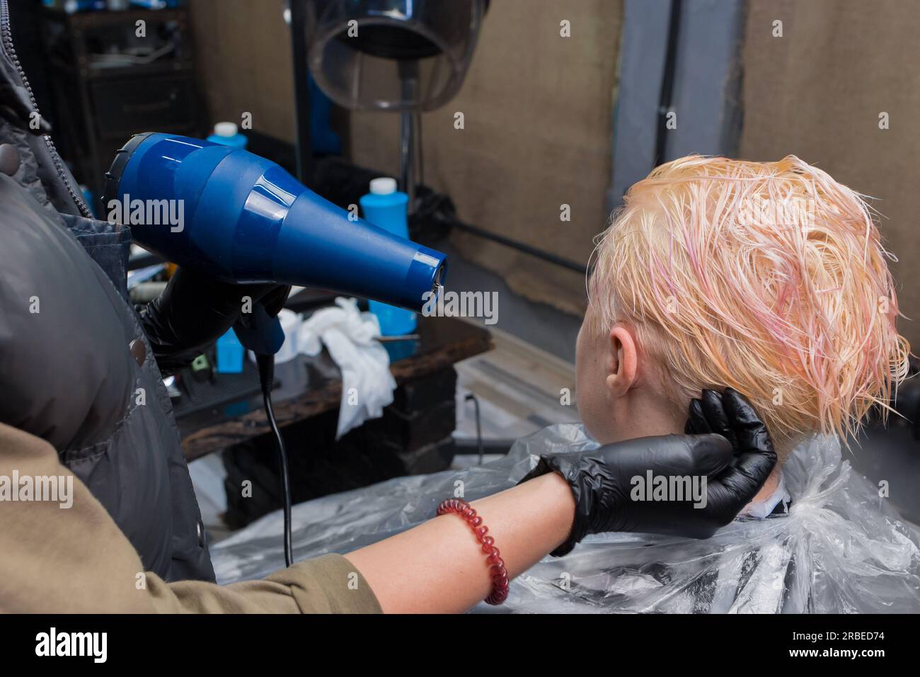 Hands in the gloves of a professional barber girl blow dry the hair of ...