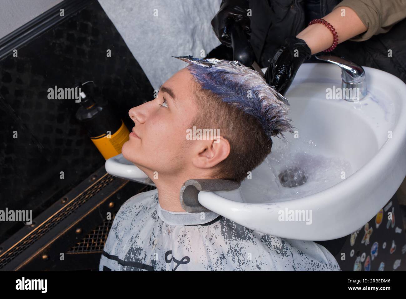 Young European handsome guy washing his hair over the sink in the salon ...
