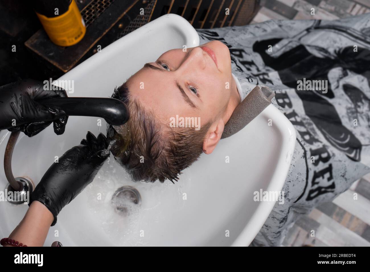 The hands of a salon worker in black gloves pour rain on the hair of a ...