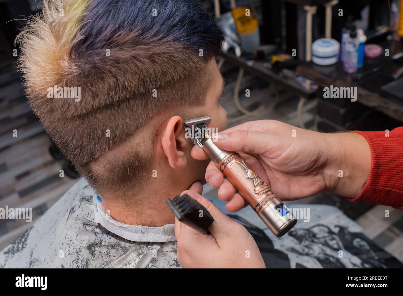 The hands of a male hairdresser in the salon shave the temporal region ...