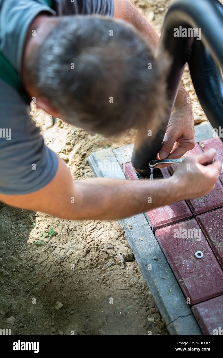 The maintenance man knelt down and bolted the leg from the park bench ...