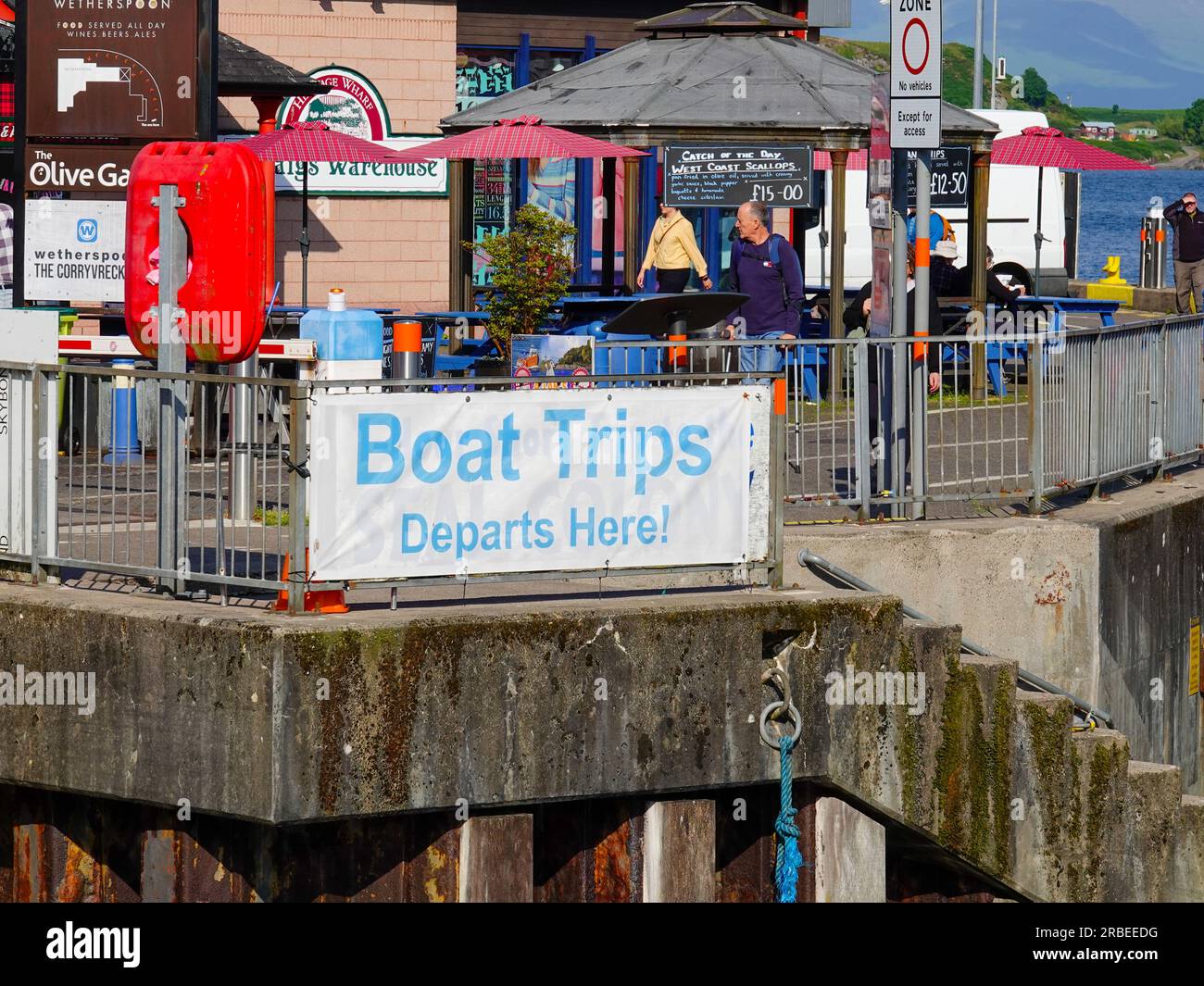 People walking in the docks area past ”Boat Trips Depart Here" sign ...
