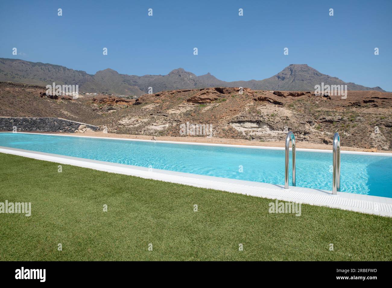 Luxurious long swimming pool overlooking the arid volcanic mountains ...