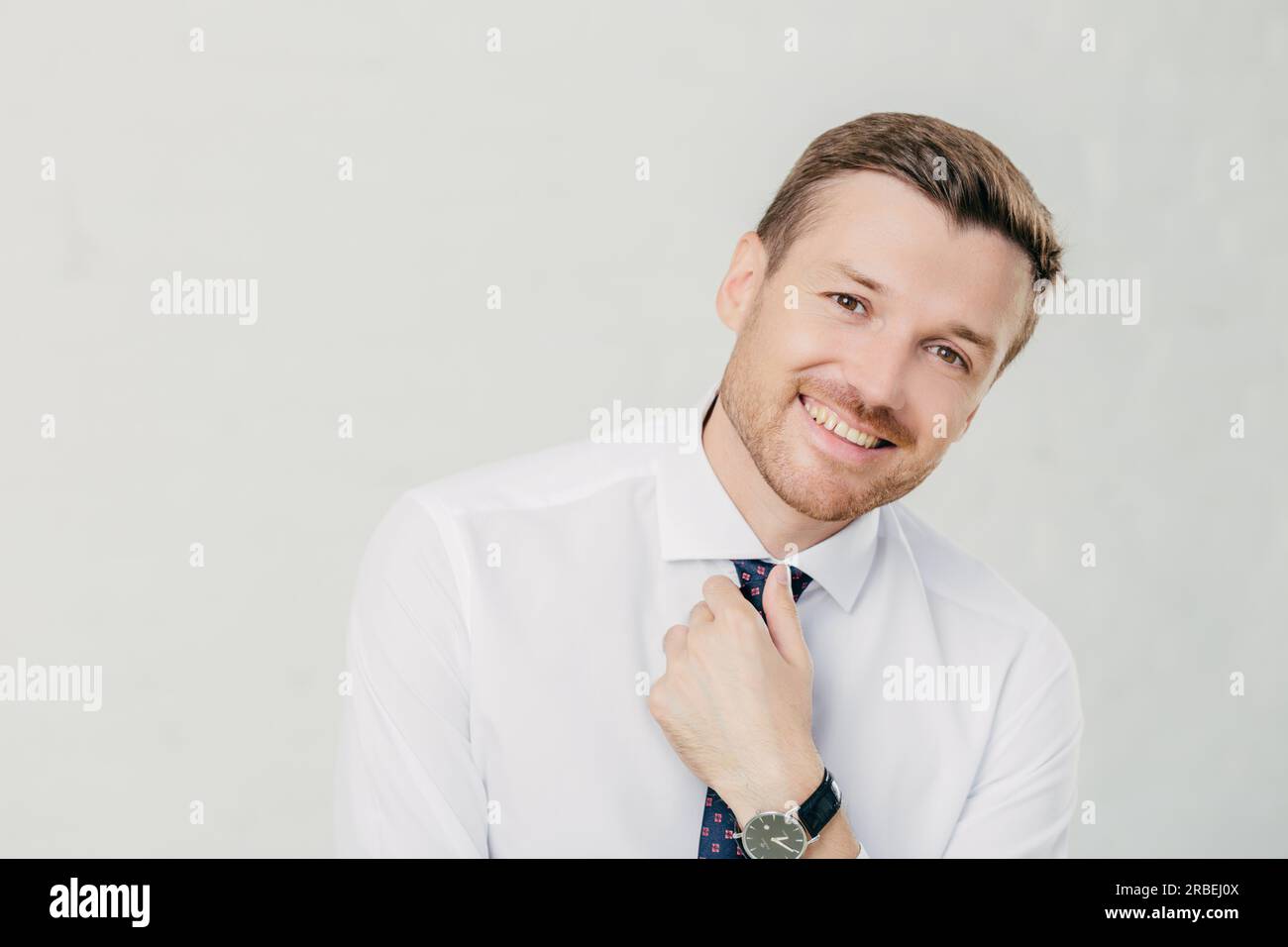 Cheerful male leader in elegant white shirt, hand on tie, smiles ...