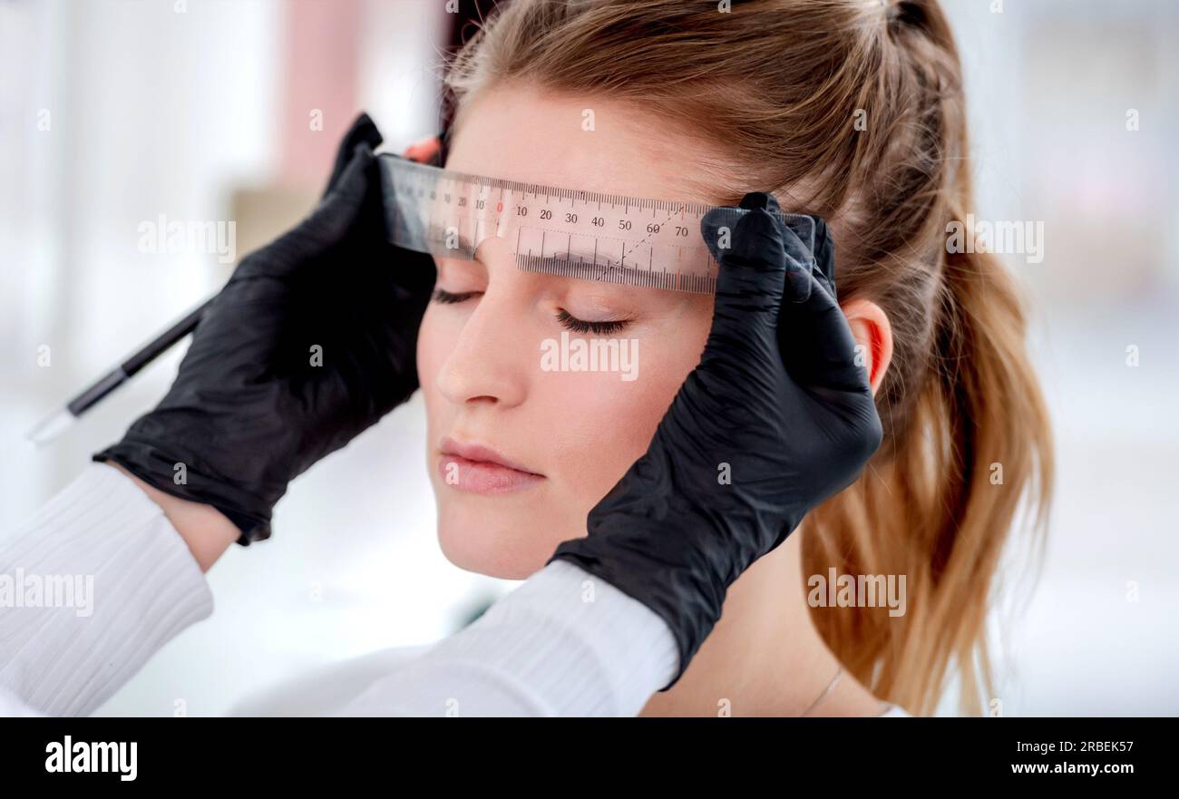 Permanent make up master measures the model forehead to draw a new ...