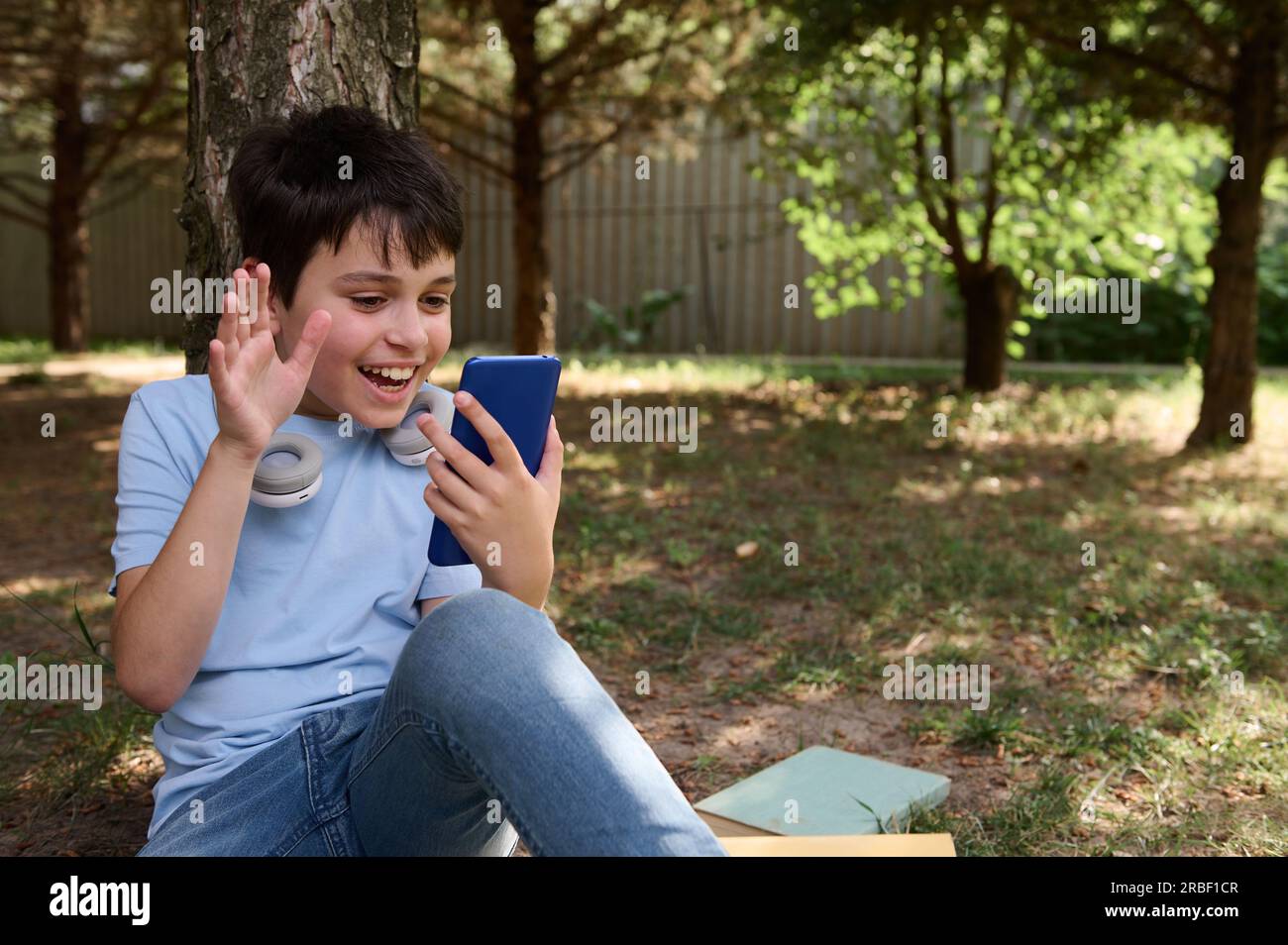 Cheerful teenage boy waving hello with his hand, smiling while having ...