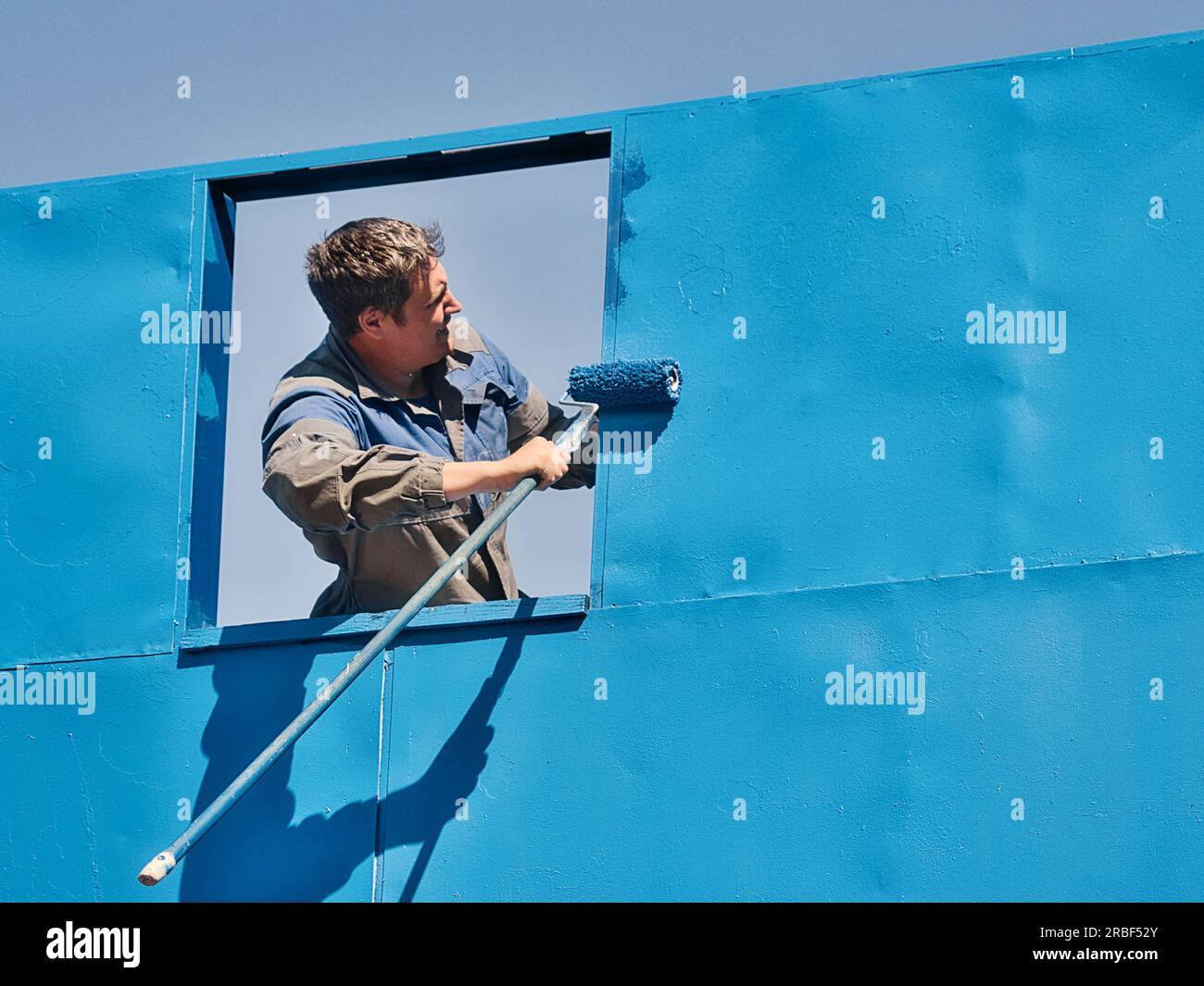 Professional painter in overalls paints metal wall of building with ...