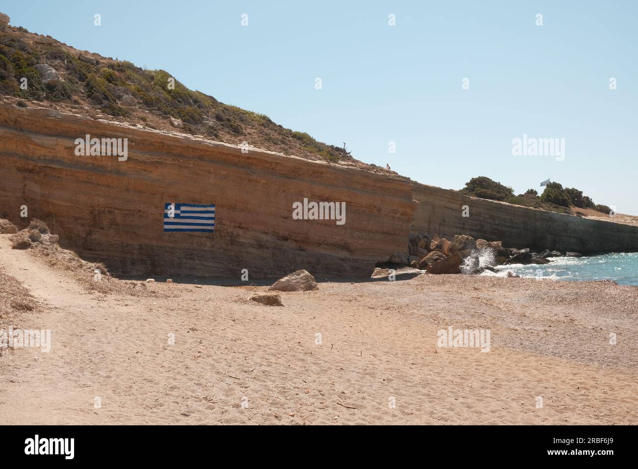 View of the Greek flag at the cliff from the Fourni Beach. Island of ...