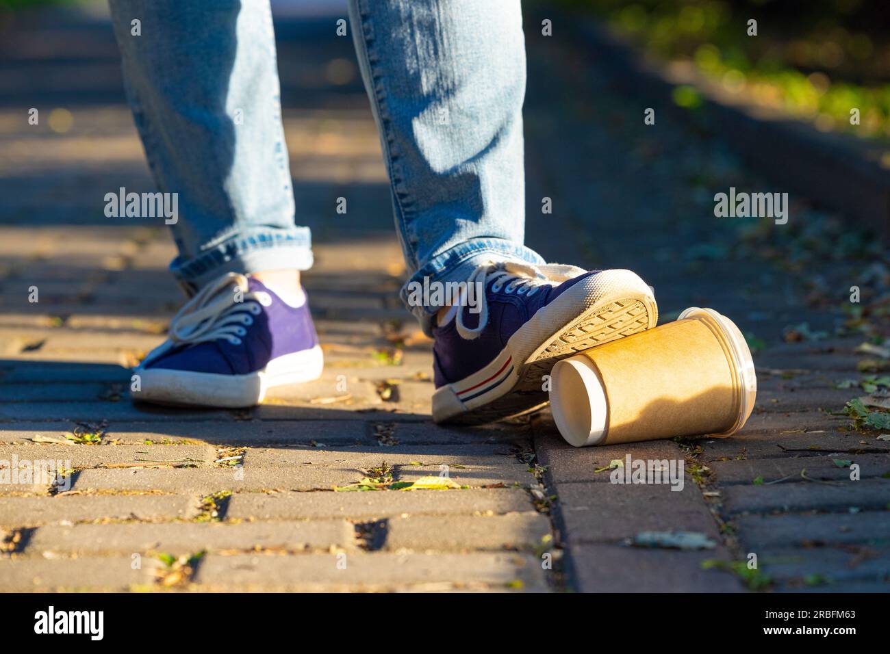 a man's foot steps on a paper cup lying on a path in the park. man ...