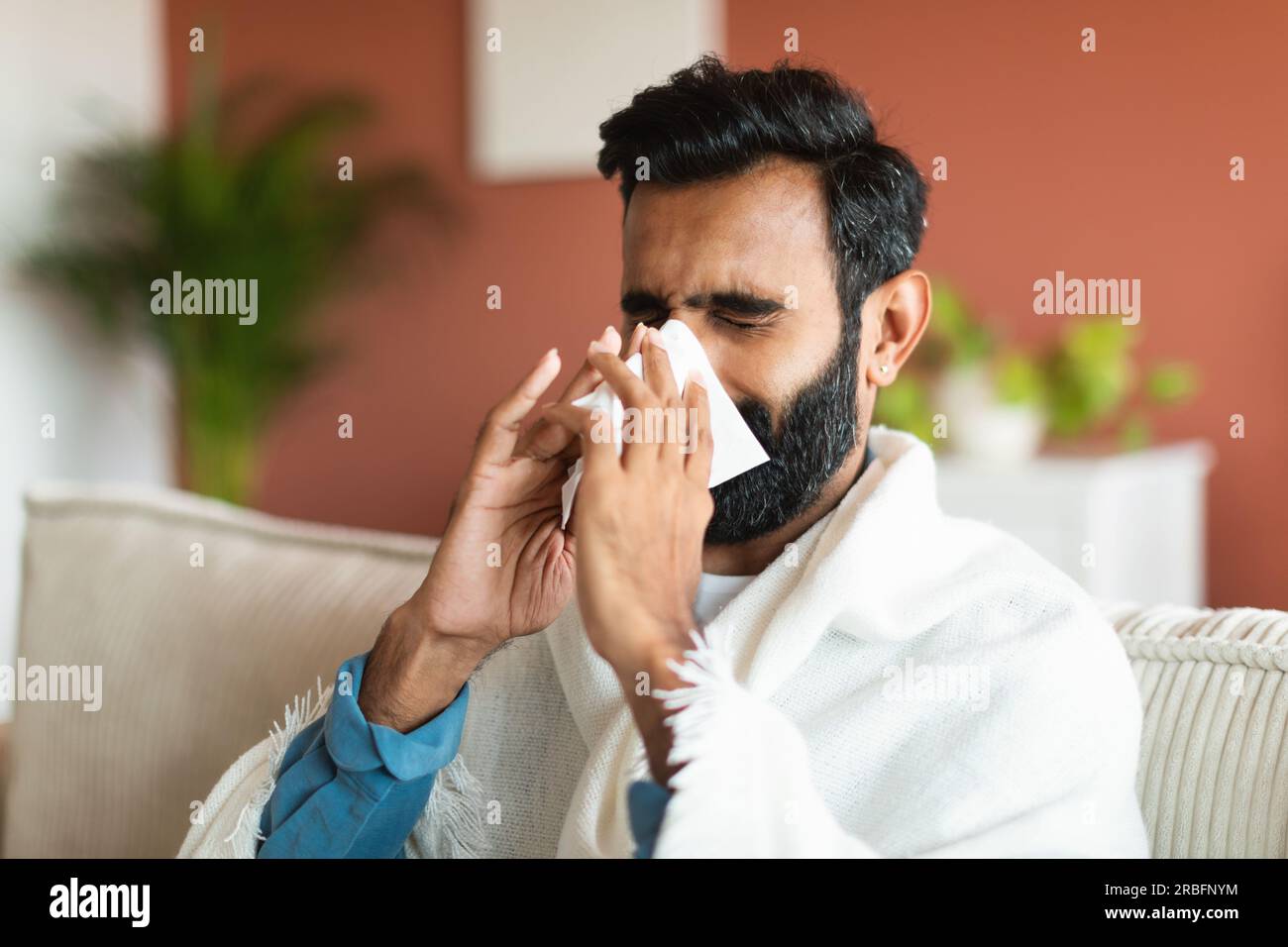 Arabic guy sneezing blowing runny nose in tissue at home Stock Photo ...