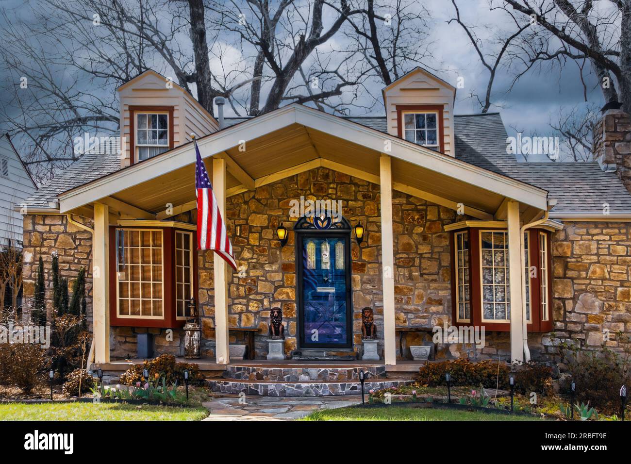 Rock two story house with bay windows and large porch lit up under dark ...