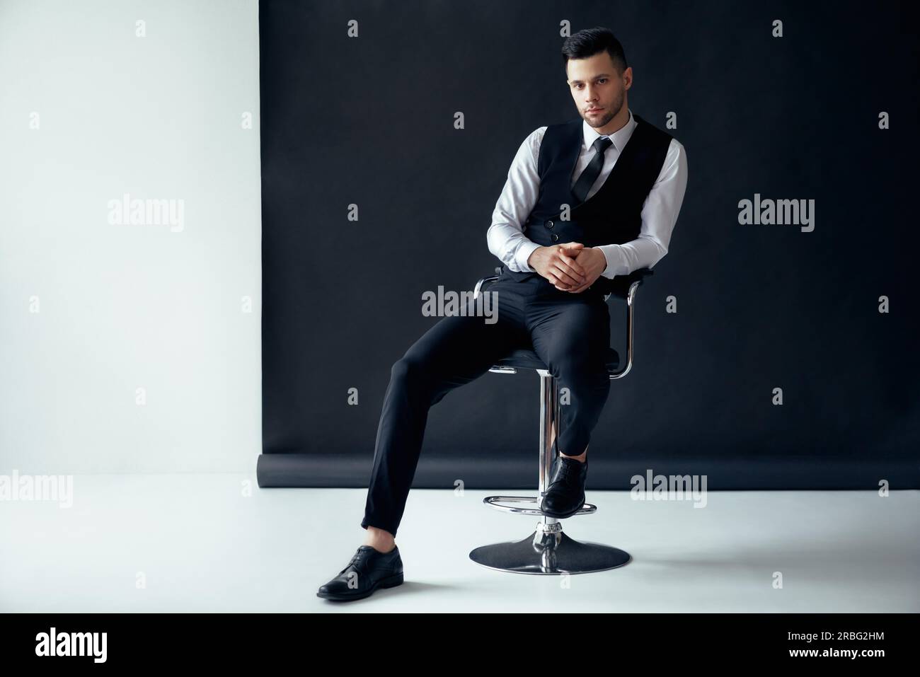 Elegant confident man posing and sitting on chair on black and white ...