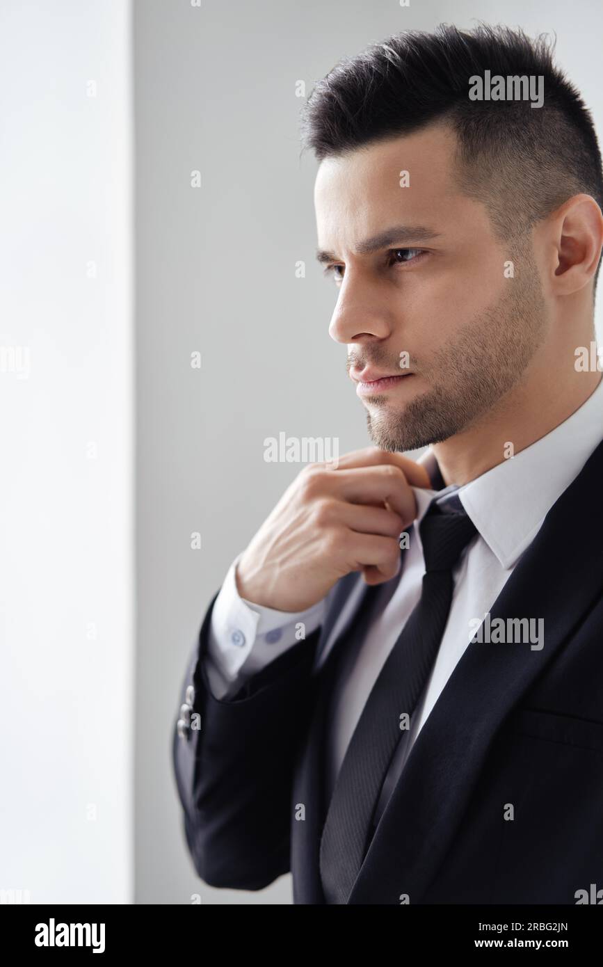 Young handsome man in elegant suit adjust his necktie on white ...