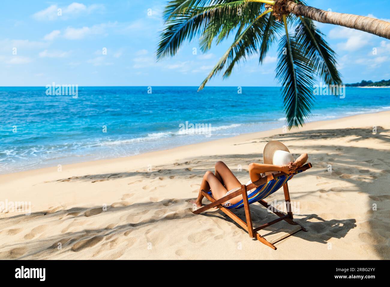 Back view of young beautiful woman sunbathe and relax on tropical beach ...