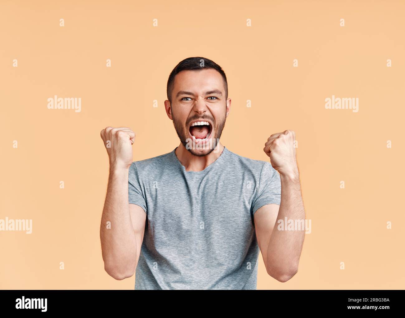 Happy man celebrating his success with winner gesture on beige ...