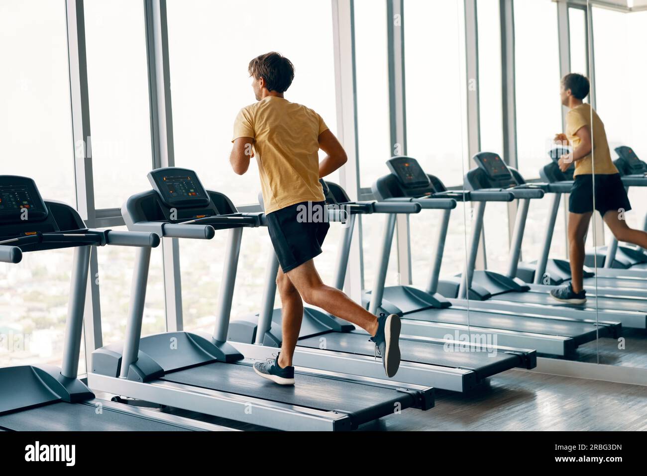 Full length portrait of young sports man running on a treadmill at gym ...