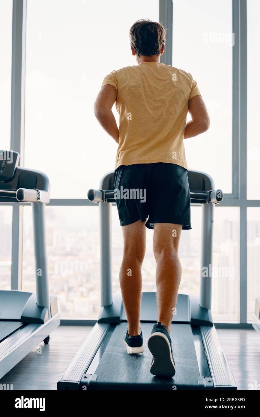 Full length portrait of young sports man running on a treadmill at gym ...