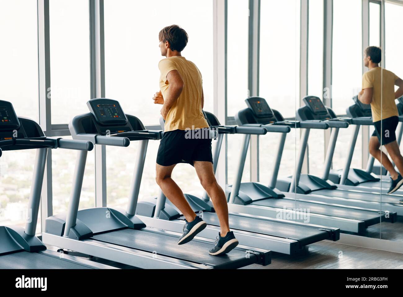Full length portrait of young sports man running on a treadmill at gym ...