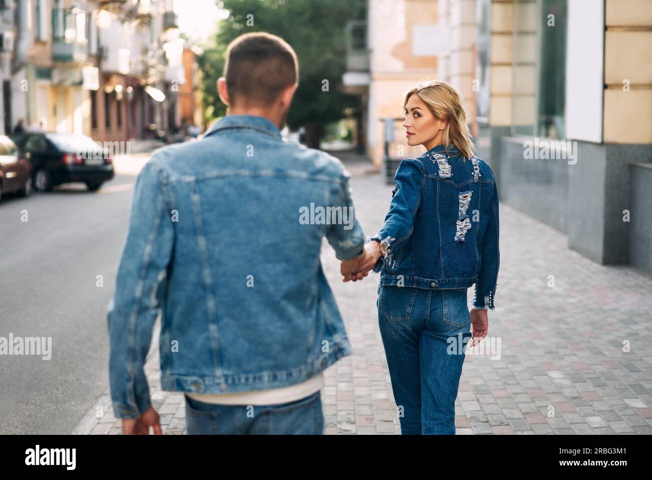 Beautiful young woman walking on the street and holding man by hand ...
