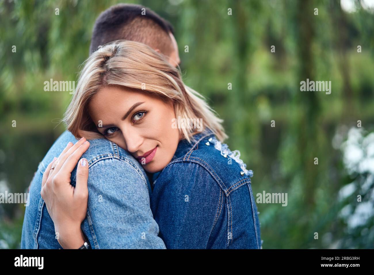 Young beautiful woman hugging her boyfriend with love outdoors. Caucasian couple in park ...