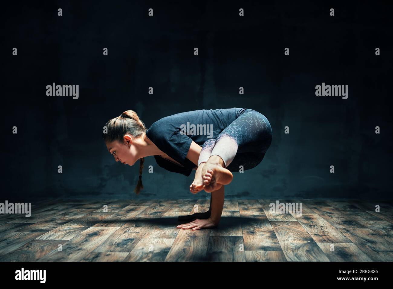 Young attractive woman practicing yoga doing side crane pose in dark ...